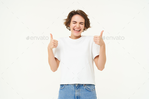 Portrait of cheerful young woman, shows thumbs up in approval, like ...