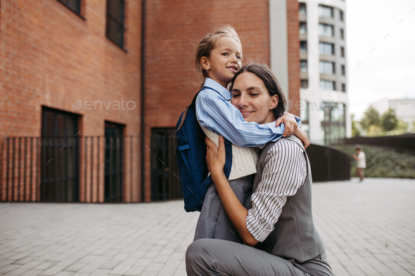 Working mother hugging daughter in front of the school building, and ...