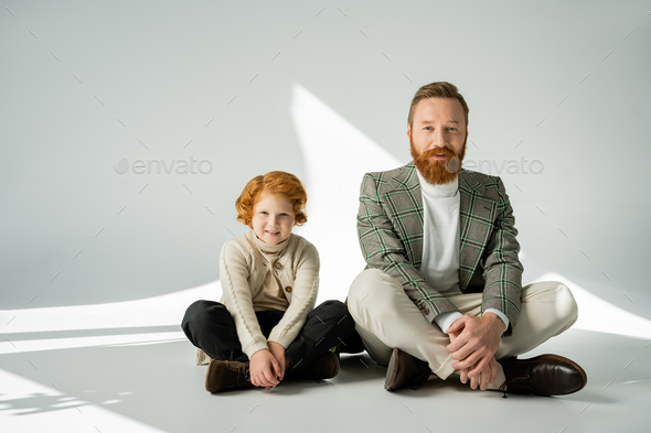Redhead boy and stylish dad sitting on grey background with sunlight ...