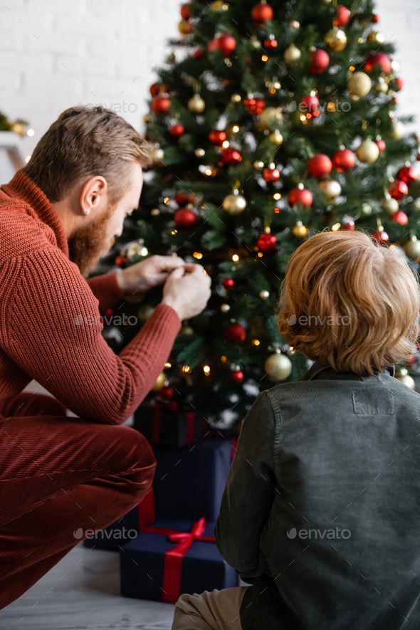 back view of redhead dad and son decorating blurred Christmas tree at ...