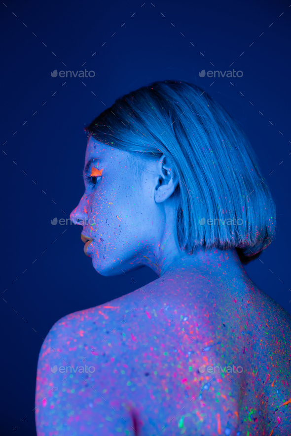 back view of young woman in glowing makeup and bright neon body paint ...