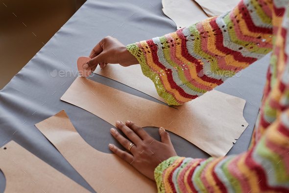 Above angle of hands of young seamstress contouring sewing pattern with ...