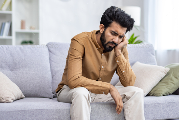 Sad depressed man sitting at home on sofa in living room, hopelessly ...