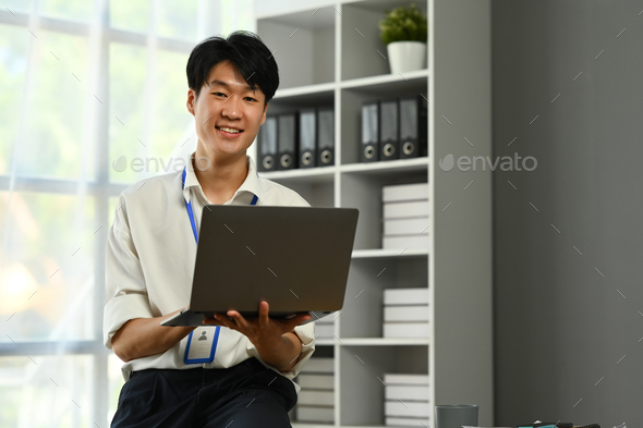 Portrait of Asian male manager sitting on desk in modern workplace and ...