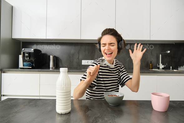Happy and emotional young woman, singing while eating breakfast, having ...