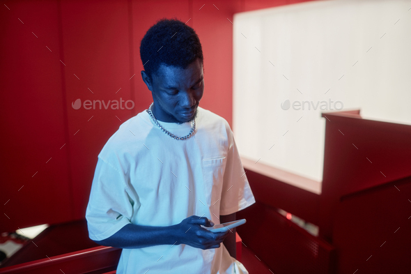 Young Black Man Holding Smartphone and Scrolling Social Media in Neon ...