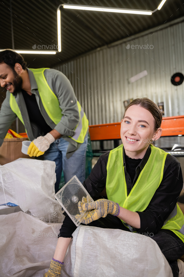 Smiling young worker in reflective vest and gloves looking at camera ...