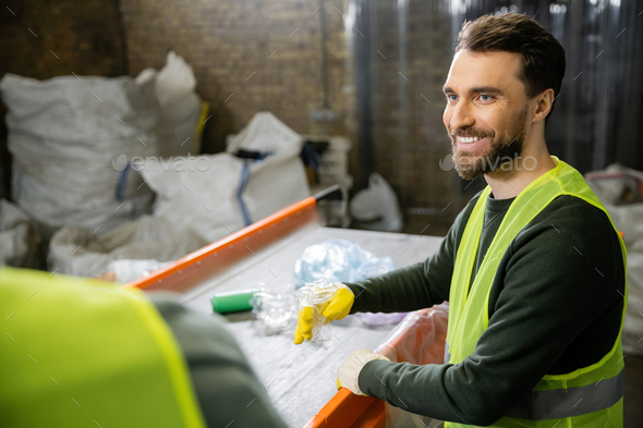 Cheerful male sorter in protective vest and gloves looking at blurred ...