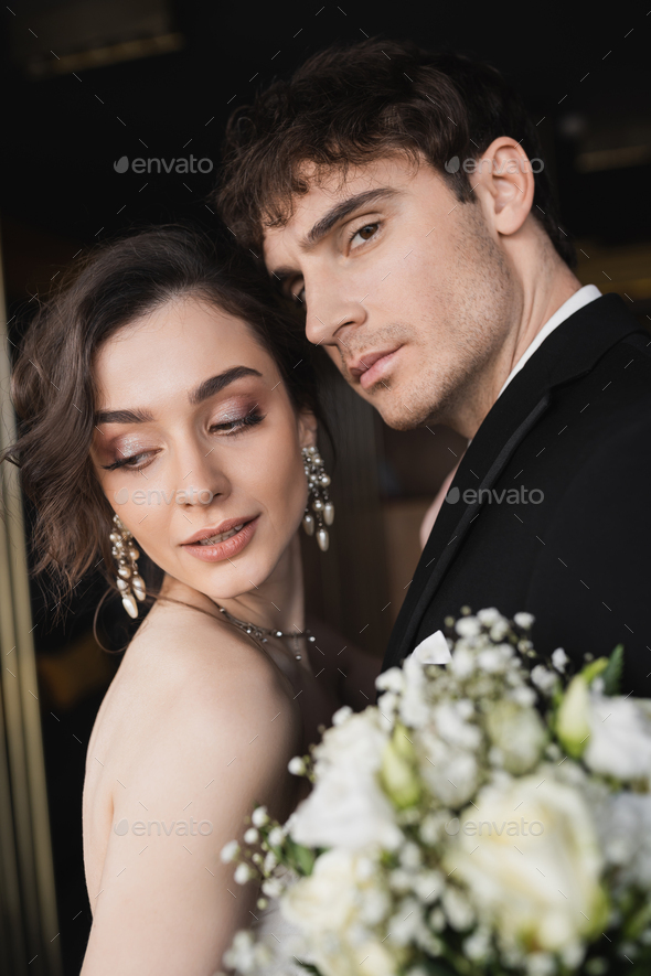 good looking groom in black formal wear standing with brunette and ...