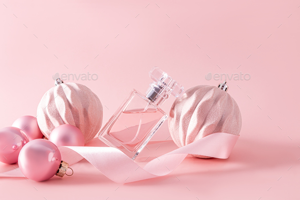 A chic bottle of women's perfume leans on a pink ball in a New Year's ...