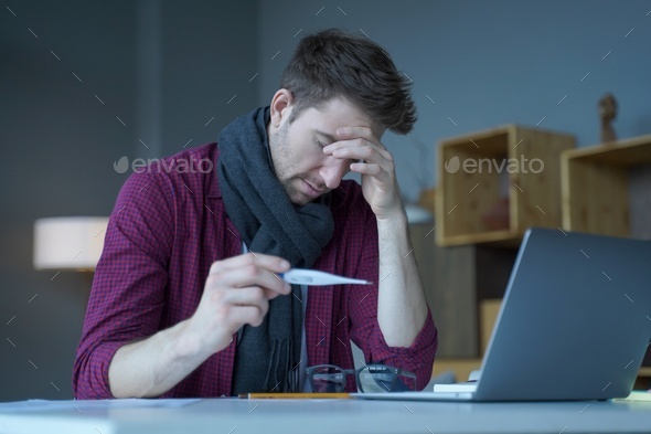 Sick man at work checking temperature with a worried look Stock Photo ...