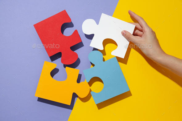 Colored paper puzzles and hand on yellow and purple background, top ...