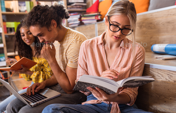 Three young students sitting on the floor in the library learning ...