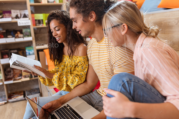 Three young students sitting on the floor in the library learning ...
