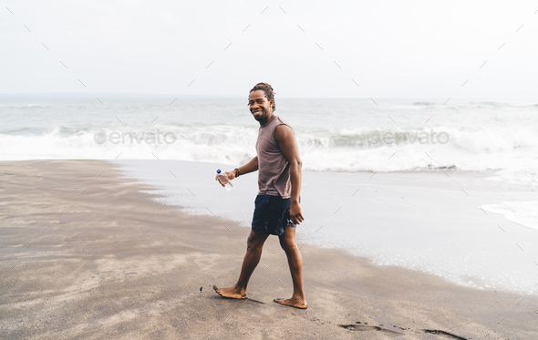 Happy black barefoot man walking along seashore Stock Photo by GaudiLab