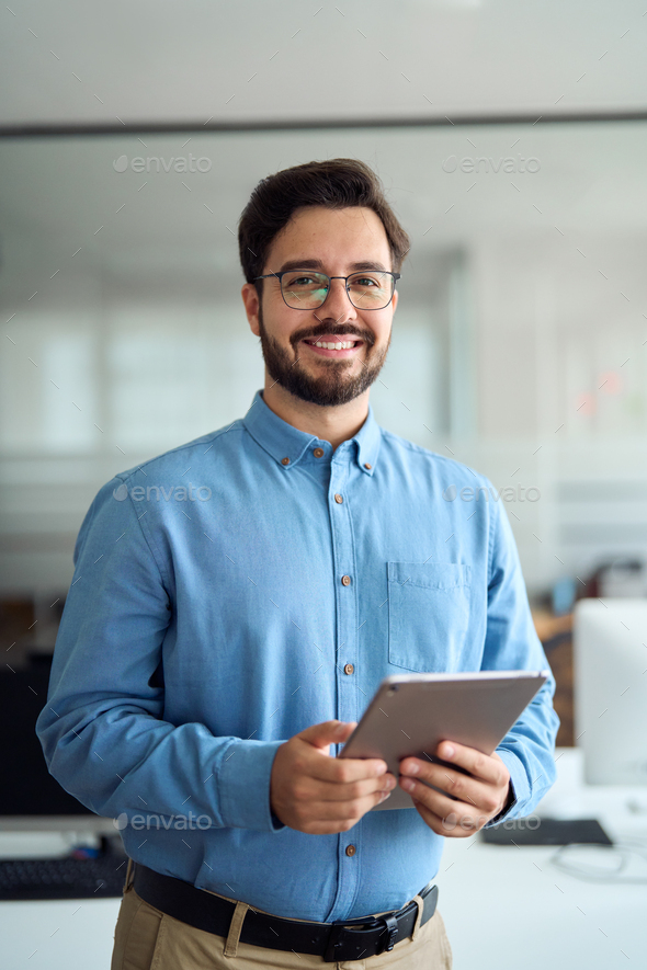 Smiling young latin business man with tab standing in office. Vertical ...