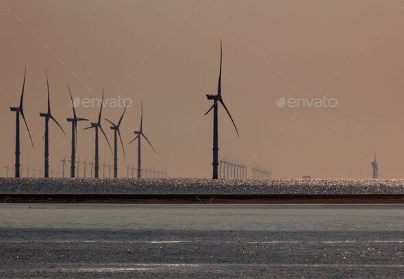 Cluster of wind turbines on a beach, illuminated by the golden light of ...
