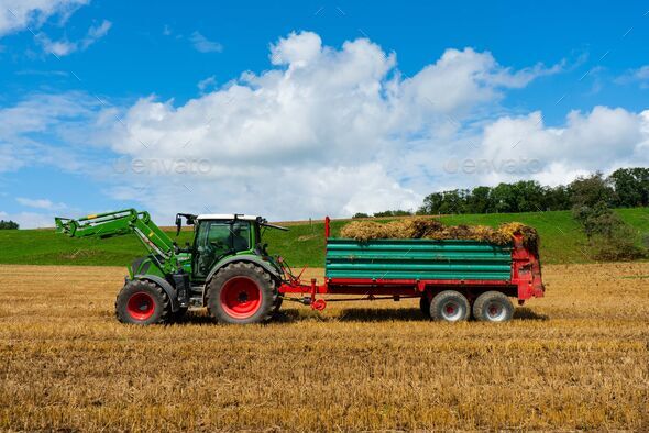 Agricultural combine, hauling a full hay wagon through a grassy field ...