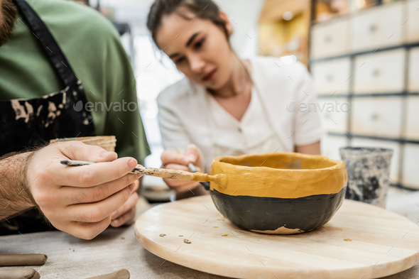 Cropped view of couple of artisans coloring ceramic bowl together in ...