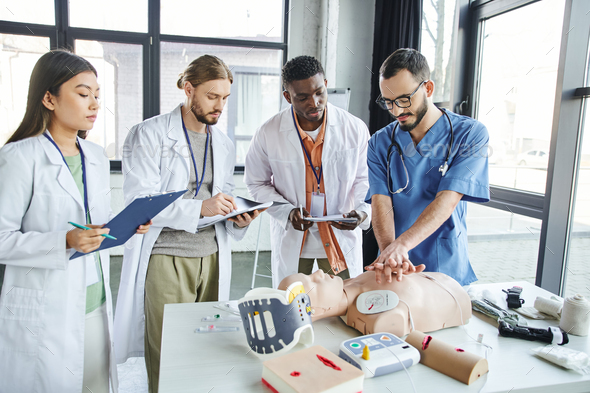 medical instructor showing chest compressions on CPR manikin near defibrillator, medical ...