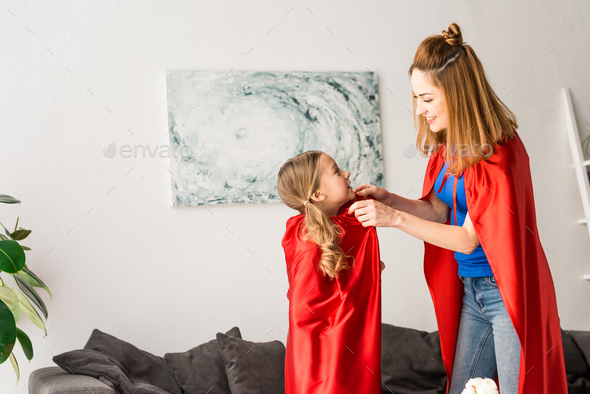 Beautiful mother tying red cloak on daughter and smiling at home Stock ...