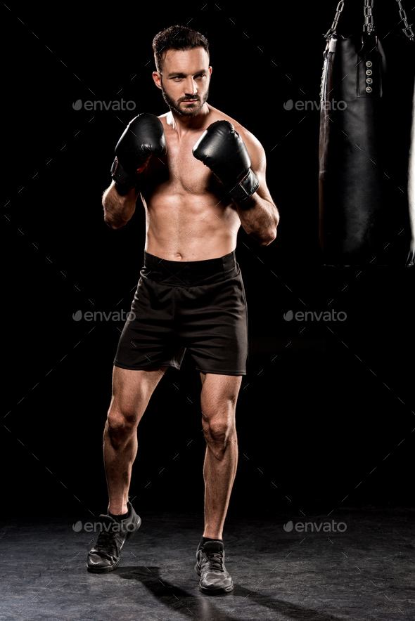 handsome athlete wearing boxing gloves standing in boxing pose on black ...