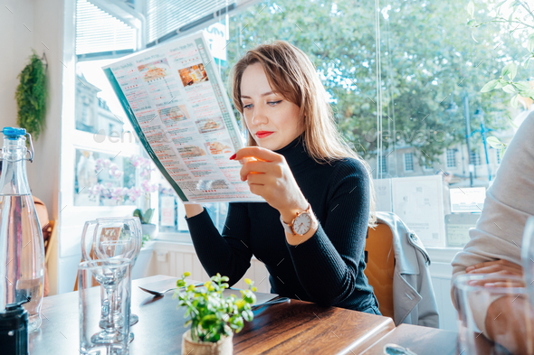 Young woman reading menu sitting with friend at casual cafe. Smiling ...