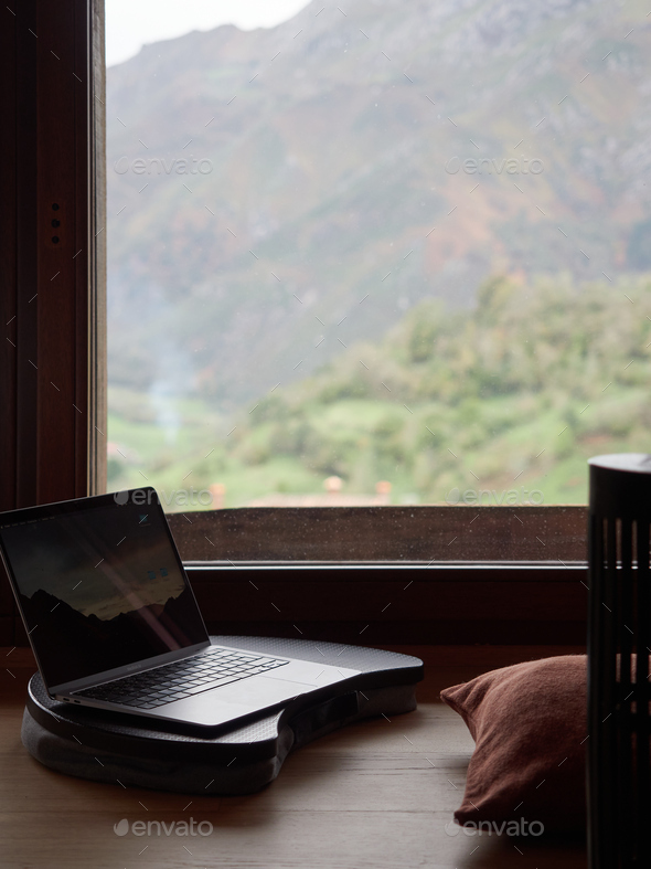Laptop on the floor next to a cushion in front of a big window with a ...