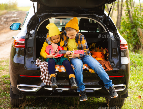 Little cute smiling girl and boy sitting in open car trunk. Kid resting ...