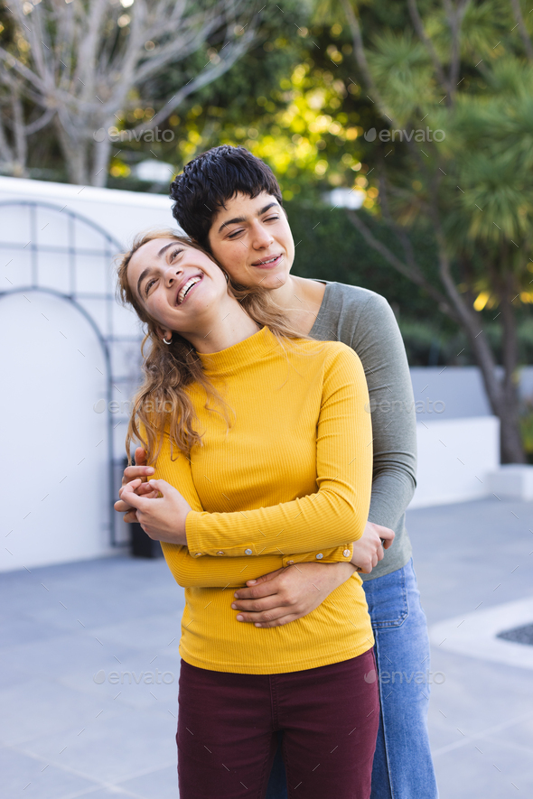 Happy Biracial Lesbian Couple Standing On Garden Terrace Embracing And