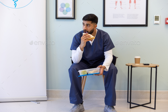 Biracial male doctor eating lunch in hospital waiting room Stock Photo ...