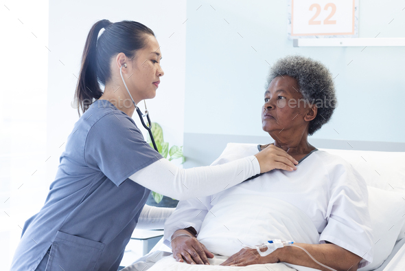 Diverse female doctor testing senior female patient using stethoscope ...