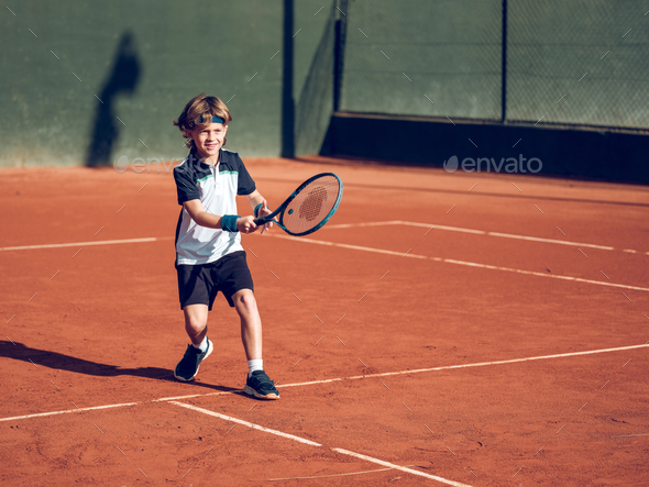 Adorable little boy running to hit ball while playing tennis Stock ...