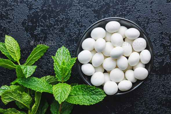 Mint candies in bowl. Menthol bonbons and mint leaves on black table ...
