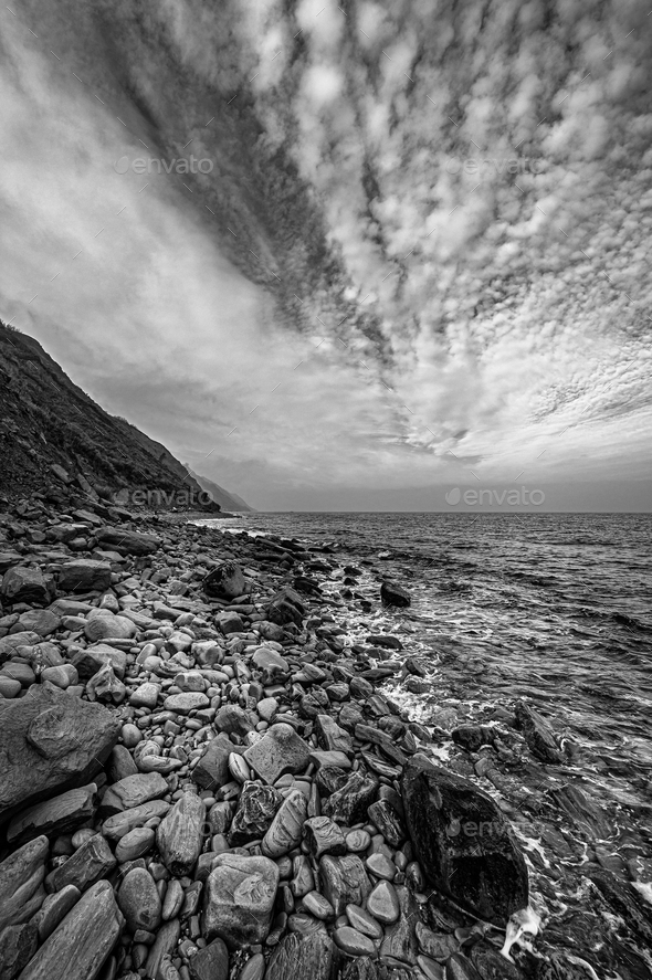 Beautiful greyscale photo of beach with pebbles, cliff, sea and cloudy ...
