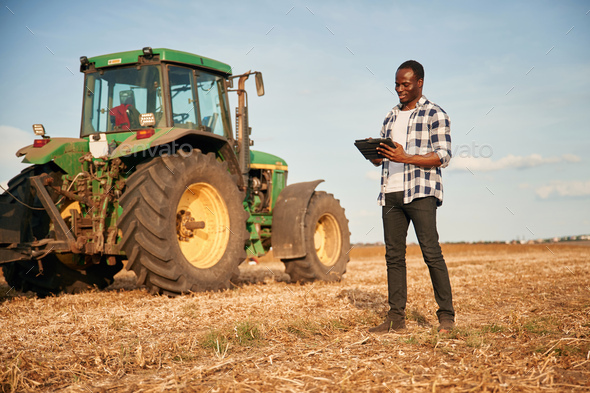 The tractor is parked behind. Beautiful African American man is in the ...
