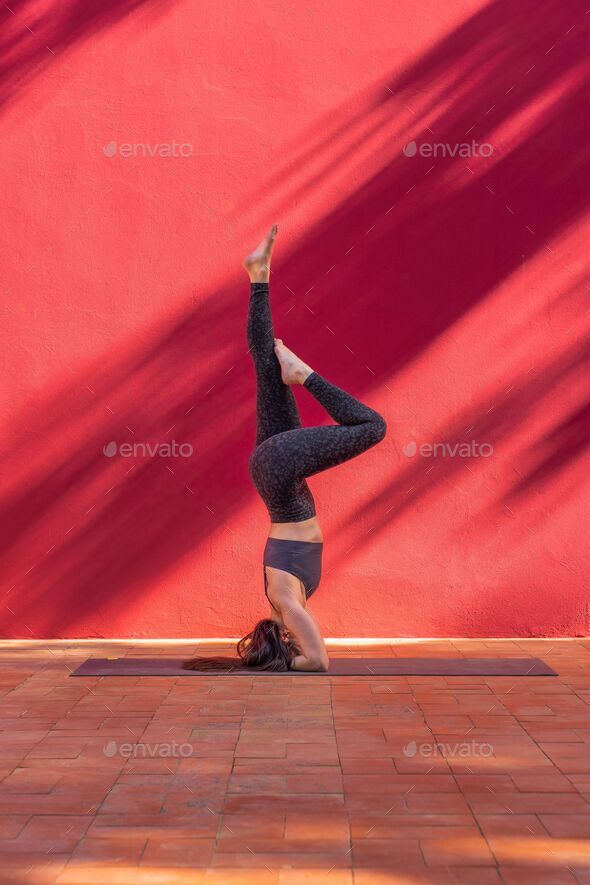 Woman performing sirsasana or headstand yoga posture on red background ...