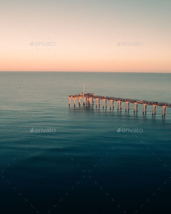 Vertical view of a pier in the ocean with sunset in the background ...