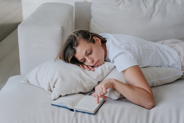 sad young tired girl is lying on a bed with an open diary, reading her ...