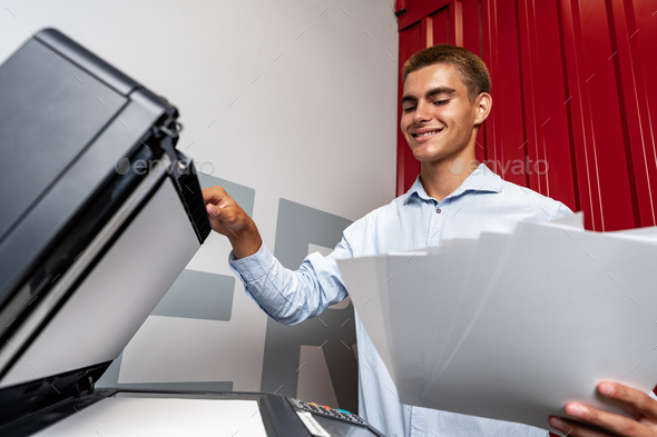 Positive young man using printer in the modern office Stock Photo by ...