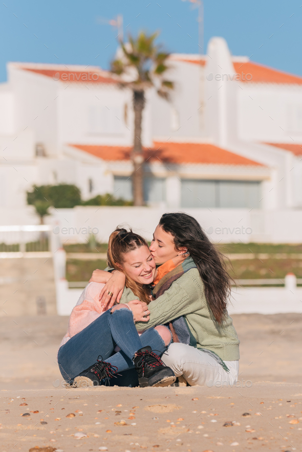 Woman kissing girlfriend on sandy beach at sunny day Stock Photo by ...