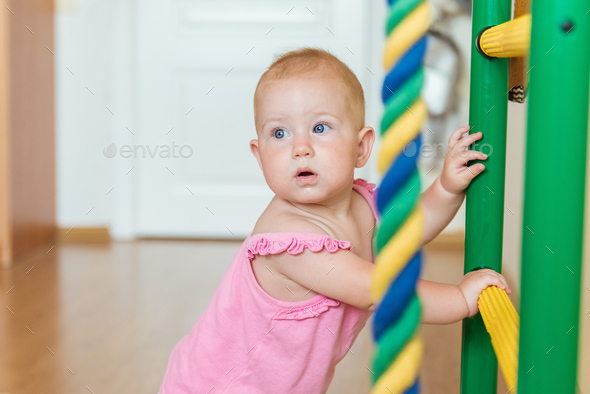 Cute baby performs gymnastic exercises on home sports complex stairs ...