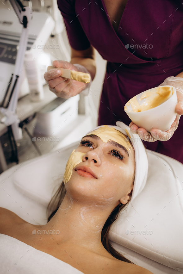 Cosmetic jelly mask, facial skincare. Cosmetologist applies yellow gold ...