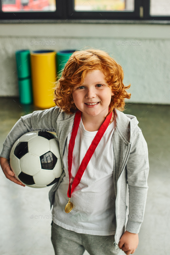 vertical shot of pretty red haired boy with golden medal holding soccer ...