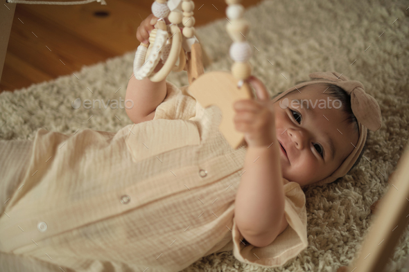 Engrossed in play, a baby reaches for wooden rings, supported by a ...