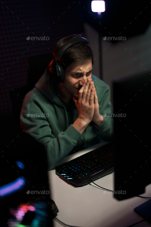 Stressed male cybersport gamer playing video game and praying with hope ...