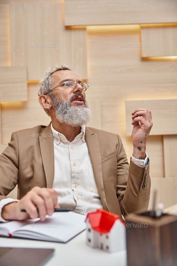 tattooed middle aged realtor in glasses talking during consultation in ...
