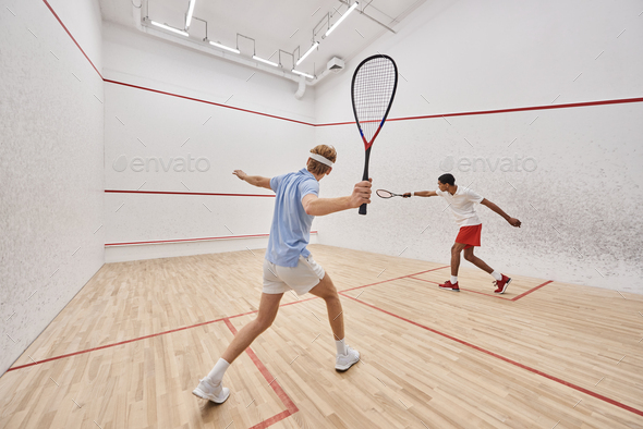 two multicultural players in sportswear playing squash together inside ...