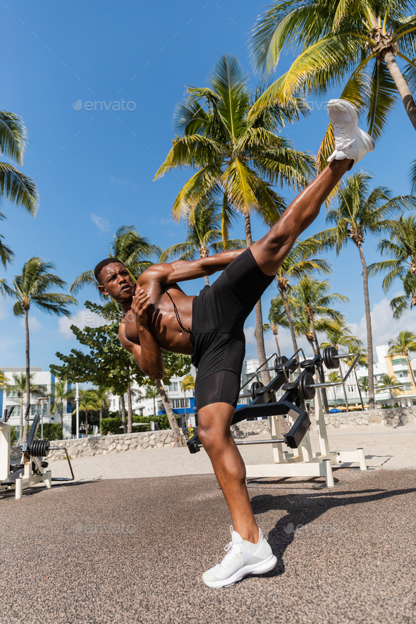 shirtless african american man in shorts doing kick exercise in Miami ...