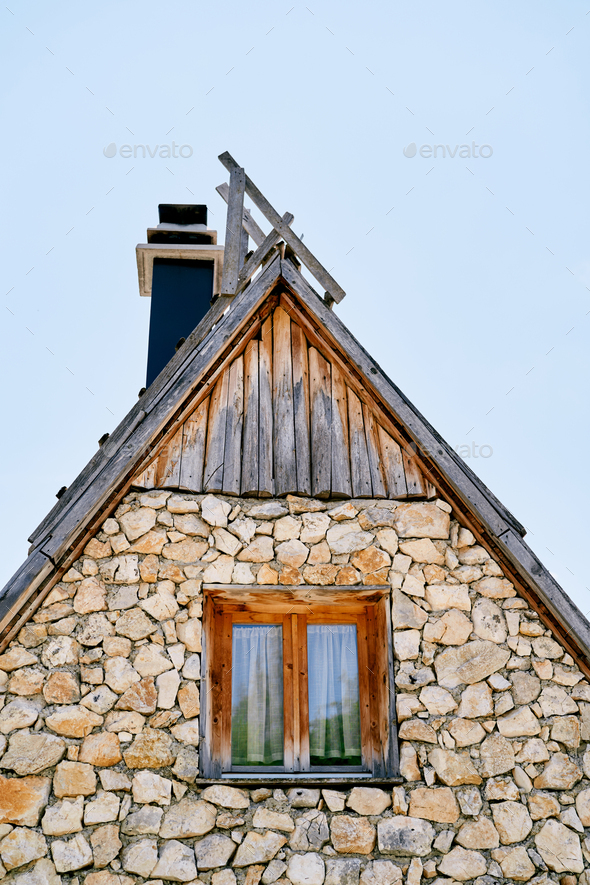 Triangular stone house with a wooden roof and a chimney against a blue ...